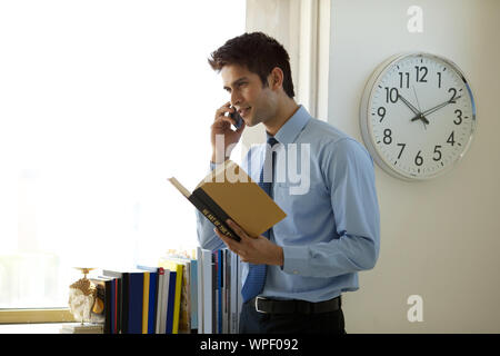 Businessman reading a book while talking on his mobile phone Stock ...