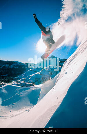 Snowboarder jumping off a cliff off piste, backlit by the sun on a ...