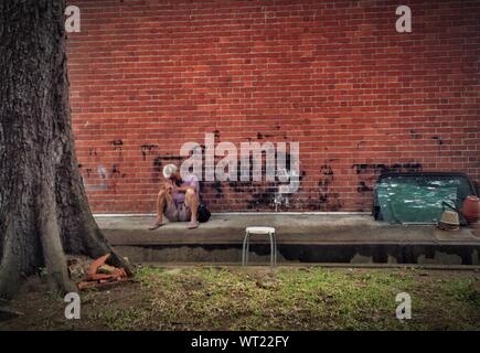 Homeless Man Sitting on Sidewalk Next to Building and Cart, East ...