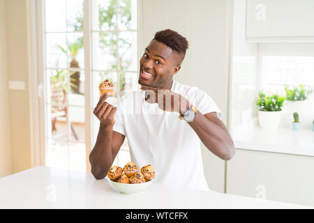 African american man eating chocolate chips muffin very happy and ...