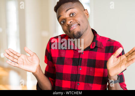 African American man at home clueless and confused expression with arms ...