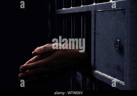 A closeup of a dimly lit prison holding cell door with arms reaching ...