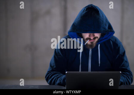 Young talented hacker smoking cigarette while working on laptop ...