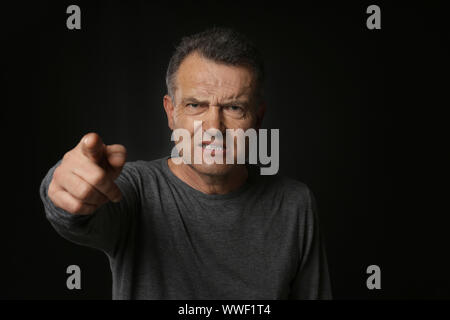 Angry mature man pointing at viewer on dark background Stock Photo - Alamy