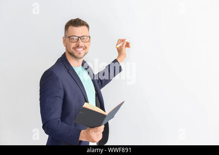 Handsome male teacher writing something on light background Stock Photo ...