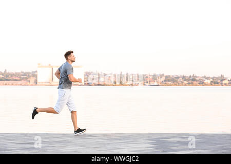 Handsome sporty man running near river Stock Photo - Alamy