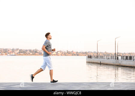 Handsome sporty man running near river Stock Photo - Alamy