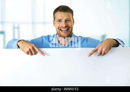 Young man pointing at blank paper sign on lilac background Stock Photo ...