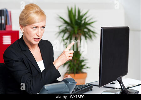 Angry woman in office indicating at computer led screen Stock Photo - Alamy
