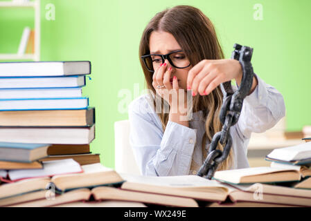Young female student chained to the desk and preparing for exams with ...