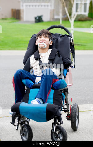 Happy disabled six year old boy waiting on sidewalk in wheelchair ...