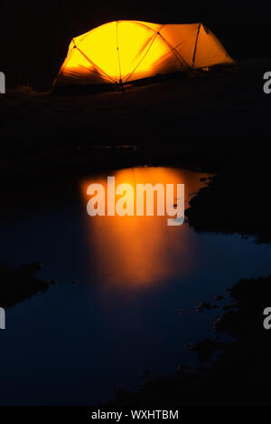 Small tent that has a light inside with the forest behind dark Stock ...