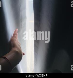 Woman moving curtain away from window Stock Photo - Alamy