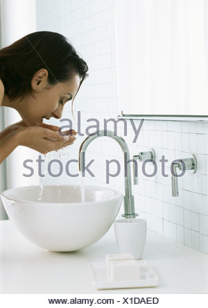 Young woman leaning over sink, hands cupped under faucet Stock Photo ...