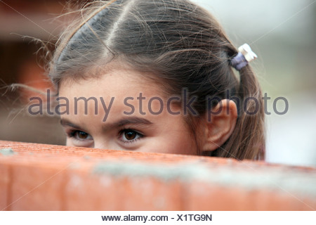 Girl peeking over a brick wall Stock Photo - Alamy