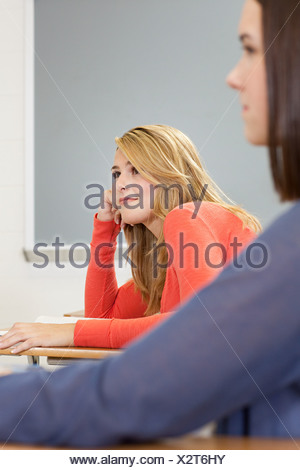 Two students sitting at desk in classroom, helping each other with ...