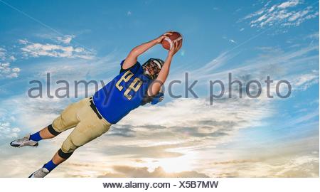 Male teenage American football player catching ball mid air against ...