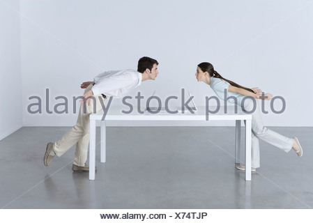 Man and woman at opposite ends of table, leaning towards each other ...