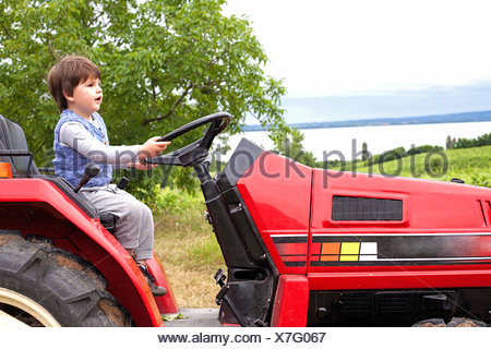 Toddler boy in the garden pretending to be a farmer driving a tractor ...
