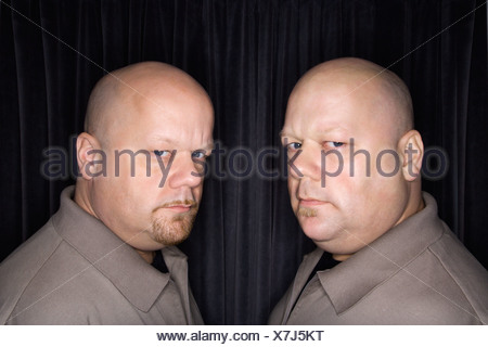 Caucasian bald mid adult identical twin men standing back to back Stock ...