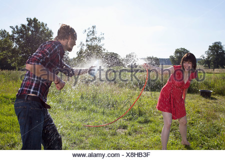 Man spraying woman with garden hose Stock Photo - Alamy