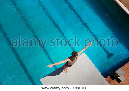 Man standing on diving board at public swimming pool above the water ...