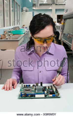 Female technician soldering electronic components in an industrial ...