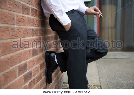 Low section of a businessmen leaning against a wall and smoking a Stock ...