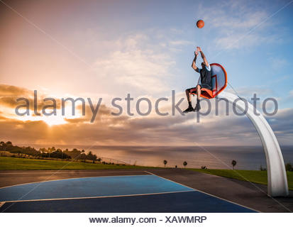 Young man sitting in a basketball hoop in a park, Los Angeles Stock ...