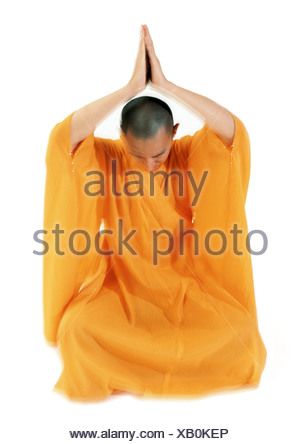 A Buddhist monk sits with his hands clasped and eyes closed chanting ...