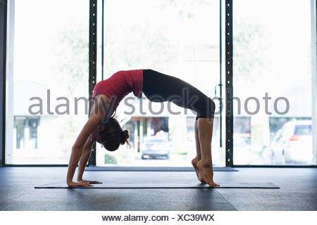 Young woman bending over backwards practicing yoga position on sea ...