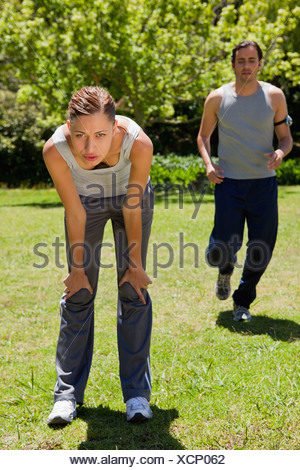Woman bending over while a man is jogging in the background Stock Photo ...