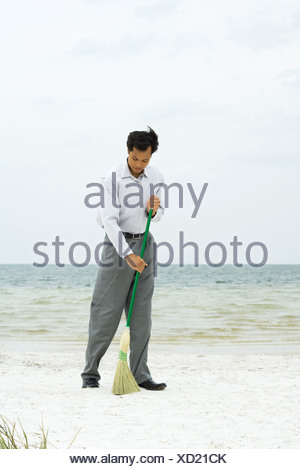 Man standing on beach sweeping with broom, full length Stock Photo ...