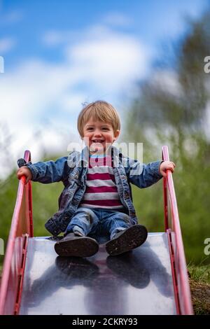 Blonde junge Kind rutscht die Rutsche auf dem Spielplatz ...