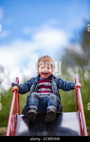 Blonde junge Kind rutscht die Rutsche auf dem Spielplatz ...