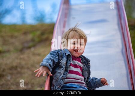 Blonde junge Kind rutscht die Rutsche auf dem Spielplatz ...