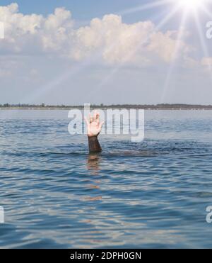 Die Hand des Mannes ragt aus dem Wasser in der Mitte des Ozeans, eine ...