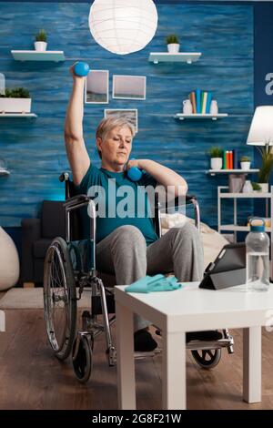Frau im Rollstuhl, die Kurzhanteln-Übungen im Fitnessstudio macht ...