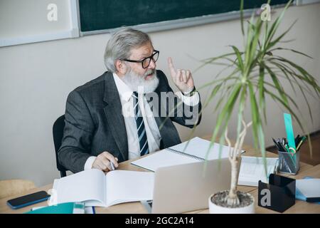 Älterer grauköpfiger Mann, Professor, Lehrer, der bei der Arbeit ...
