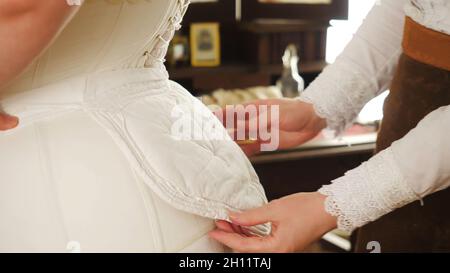 Frau im Korsett aus dem 19. Jahrhundert. Archivmaterial. Nahaufnahme der Magd hilft ihre Herrin ...