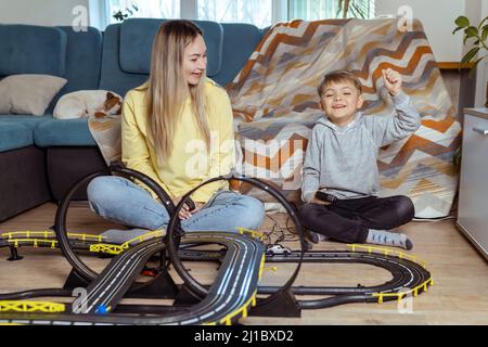 Mama und kleiner Sohn spielen zu Hause auf dem Teppich Rennen, haben ...