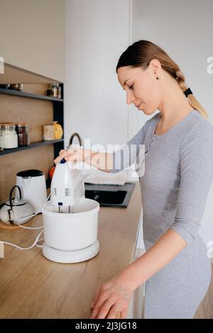 Junge Frau, die in der Küche einen Edelsteinkuchen backt, steht an der ...
