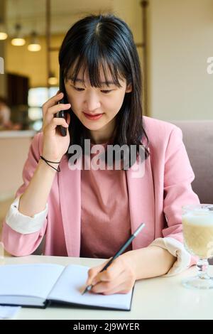 Junge seriöse Geschäftsfrau oder Freiberuflerin mit Stift über Copybook ...