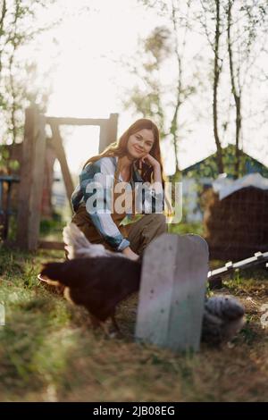 Eine Frau sitzt im Vogelfutterstall und füttert die Hühner an einem ...