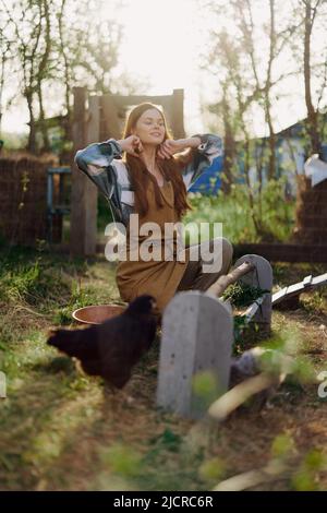 Eine Frau sitzt im Vogelfutterstall und füttert die Hühner an einem ...