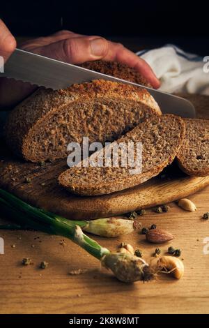 Männer schneiden ein Brot auf einem Schneidebrett auf dunkelschwarzem ...