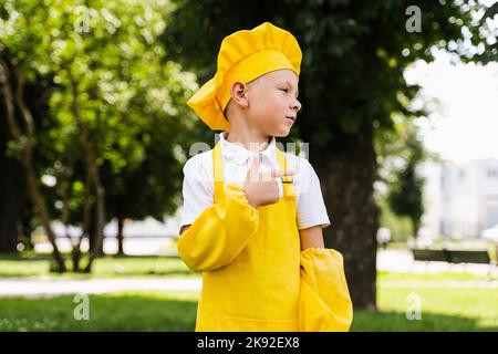 Zeigen Sie nach rechts. Schöner Koch Kind in gelben Köchhut und Schürze ...