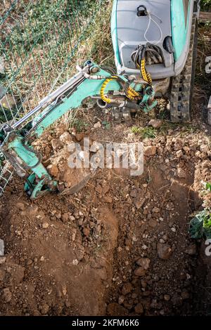 Minibagger gräbt einen Graben, um Rohre zu verlegen. Nahaufnahme eines ...