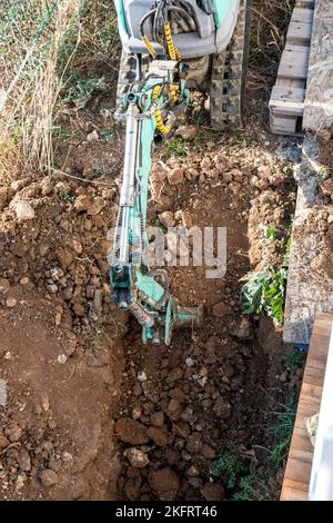 Minibagger gräbt einen Graben, um Rohre zu verlegen. Nahaufnahme eines ...