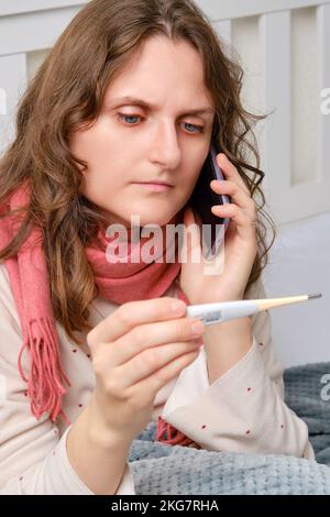 Ein krankes Mädchen sitzt eingewickelt in eine Decke mit einer Maske ...